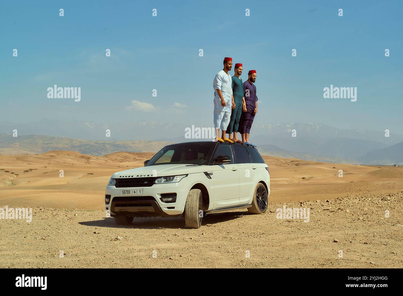 Three Arabic men stand atop a white SUV in a desert landscape with ...
