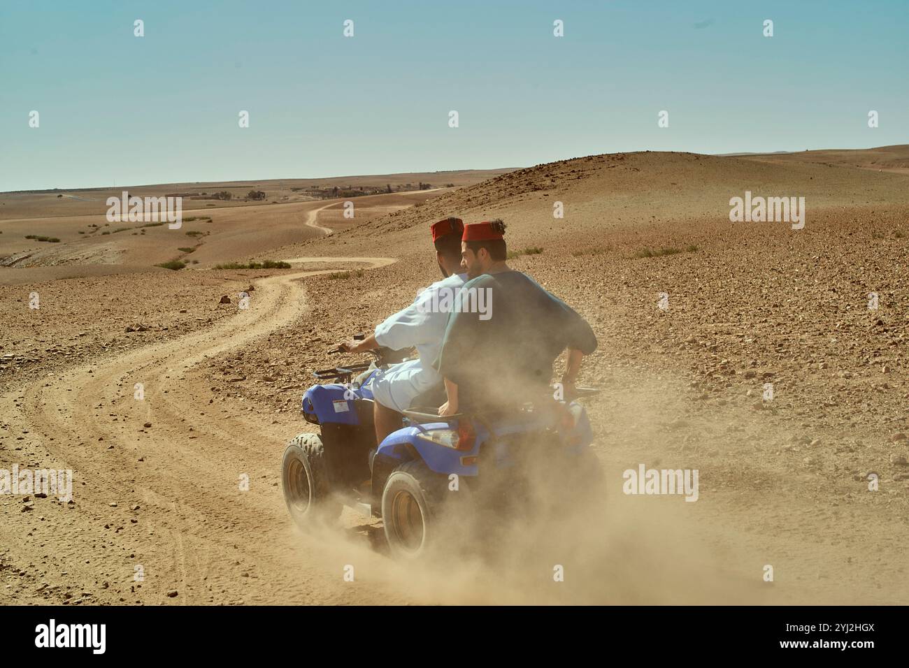 Two individuals ride a blue ATV through a desert landscape, leaving a ...
