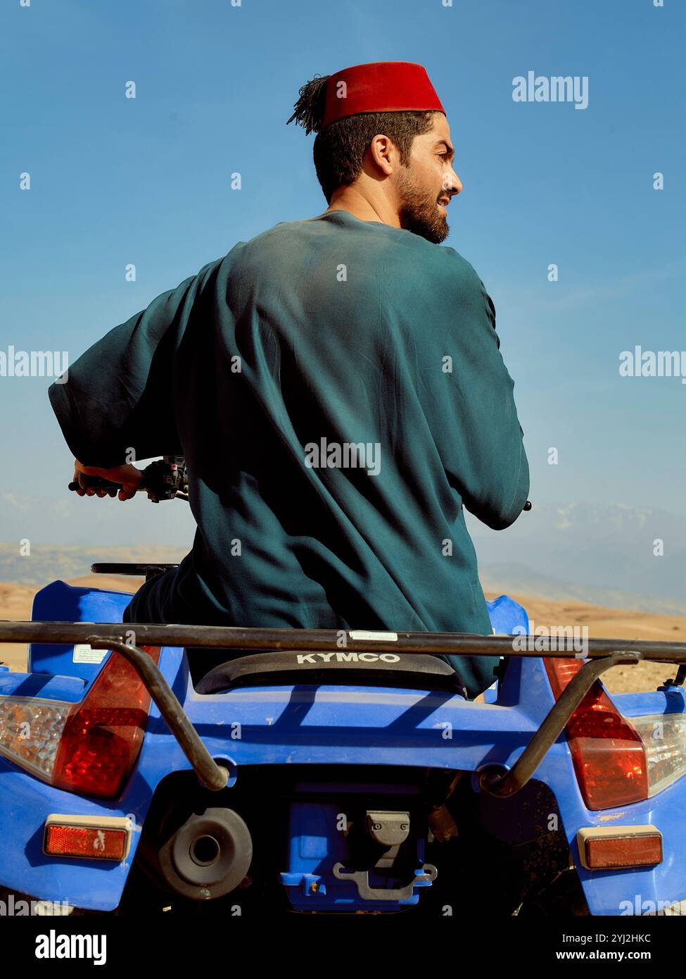 Man in traditional attire riding a blue quad bike on a clear day with a ...