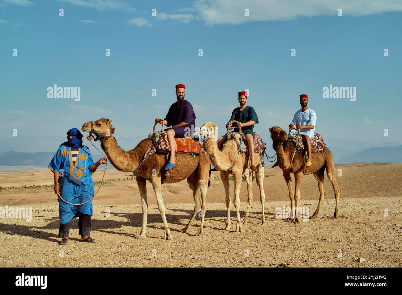 Men in traditional attire riding camels across a desert landscape under ...