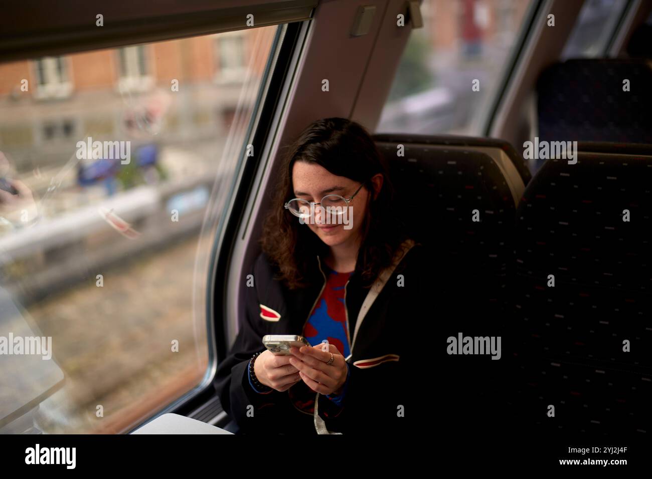 A woman smiles while looking at her smartphone in a train compartment ...