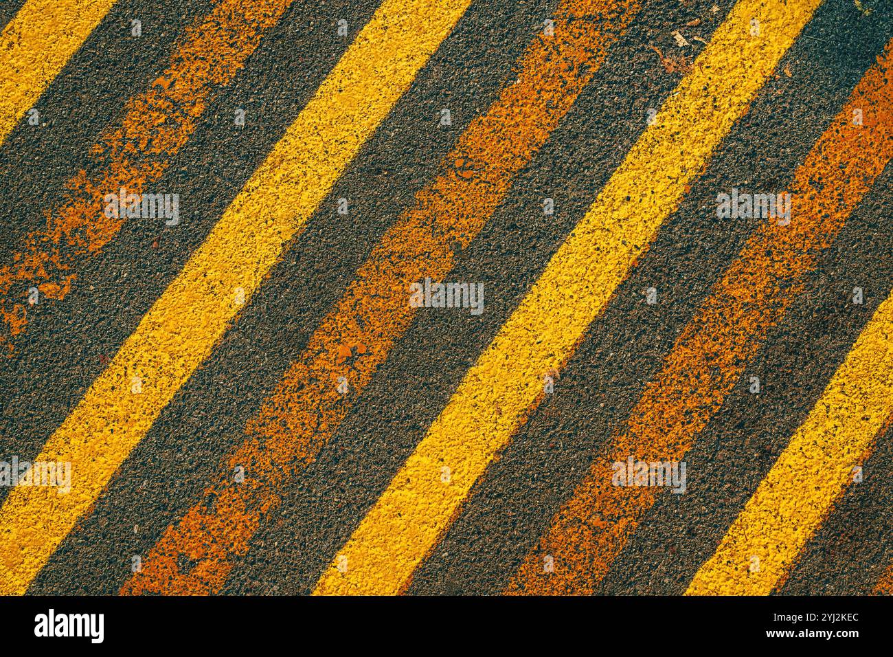 Diagonal yellow caution strip lines painted on black asphalt surface ...