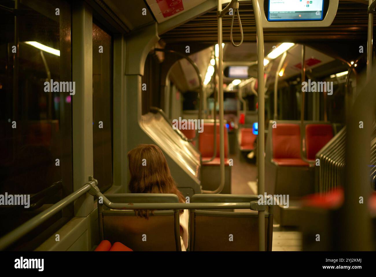 A woman seated alone on a city bus during the night with interior ...
