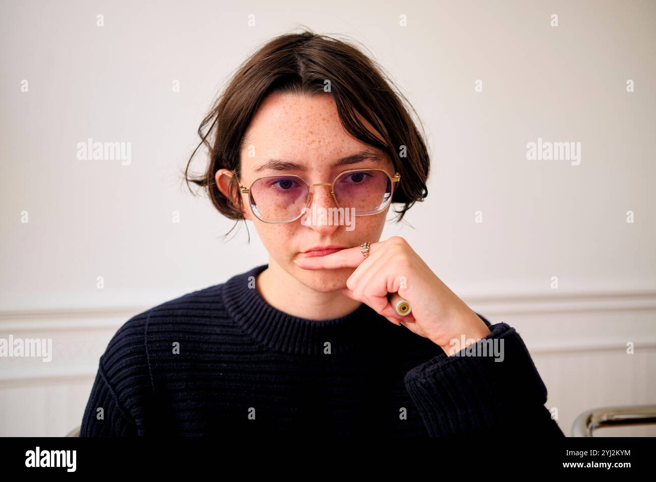 Portrait of a contemplative young woman with glasses and a navy sweater ...