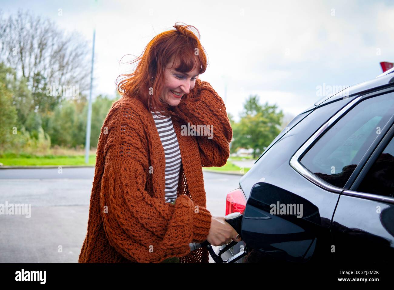 Smiling woman with red hair wearing a brown knitted cardigan fueling ...