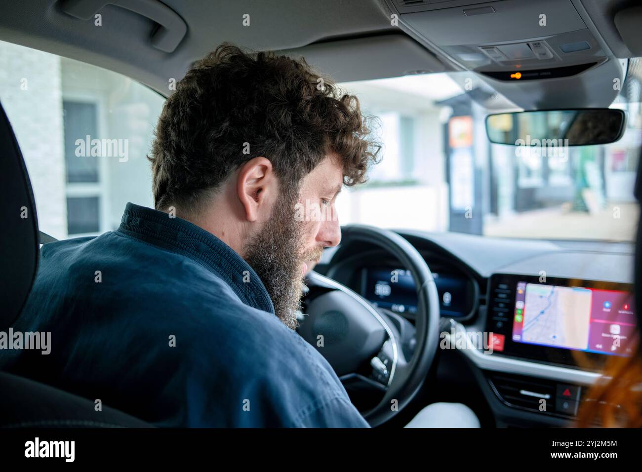 Man with curly hair driving a car, looking at the road ahead with a ...