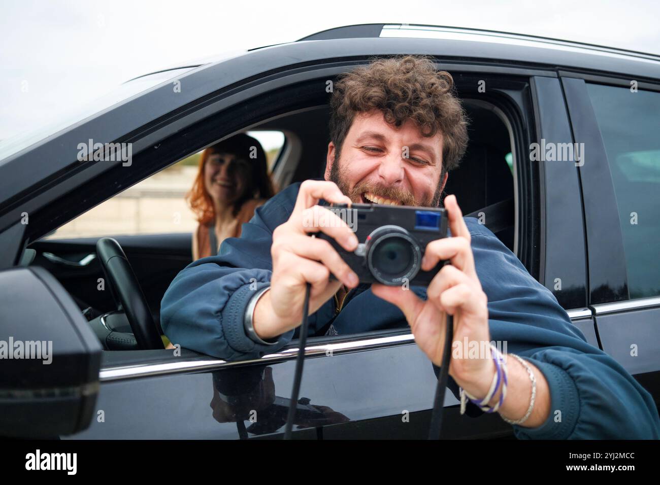Smiling man with a camera takes a photo from the driver's seat of a car ...