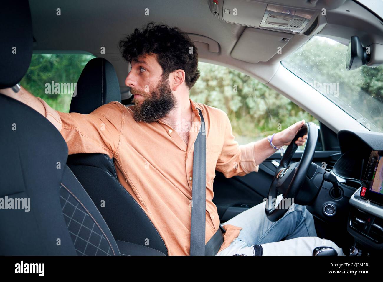 A bearded man driving a car looks back with a puzzled expression Stock ...