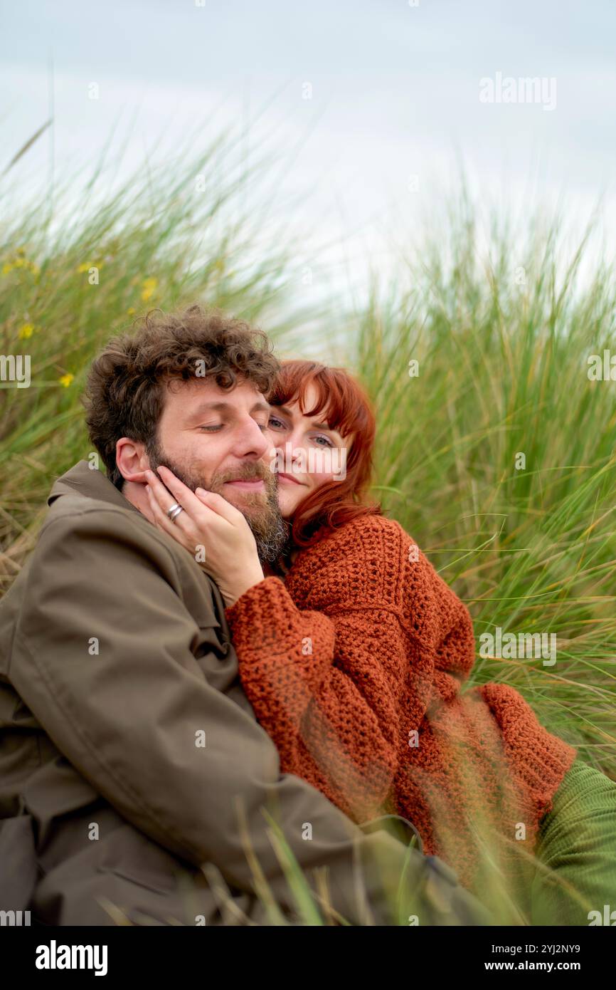 A couple embraces tenderly among tall grass, with a woman resting her head on a man's shoulder ...