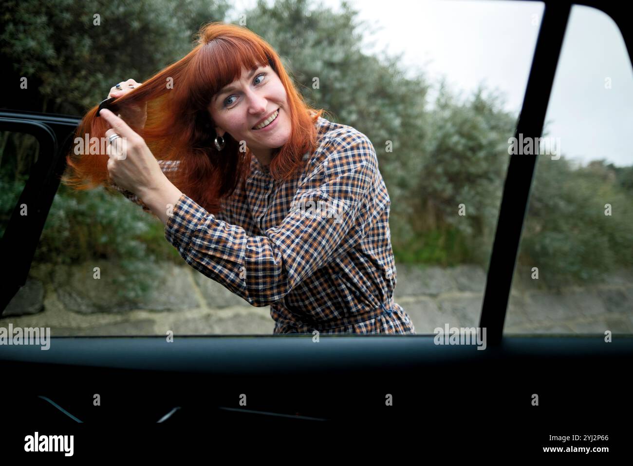 Smiling woman with red hair looking into a car window, brushing her ...