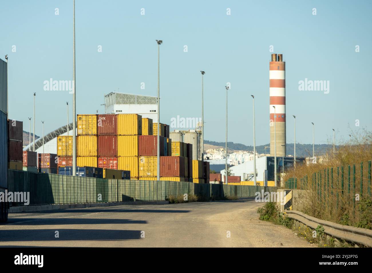 Colorful cargo containers stacked high near a tall industrial chimney ...