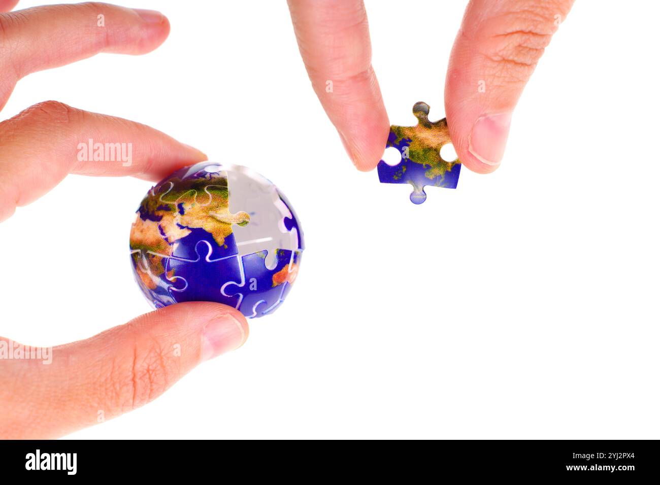 Hands assembling a jigsaw puzzle piece into a globe. Focus on global ...