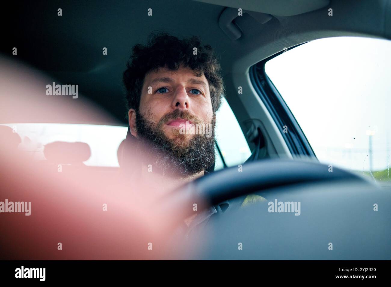 Bearded man with curly hair driving a car, viewed from the passenger side Stock Photo - Alamy