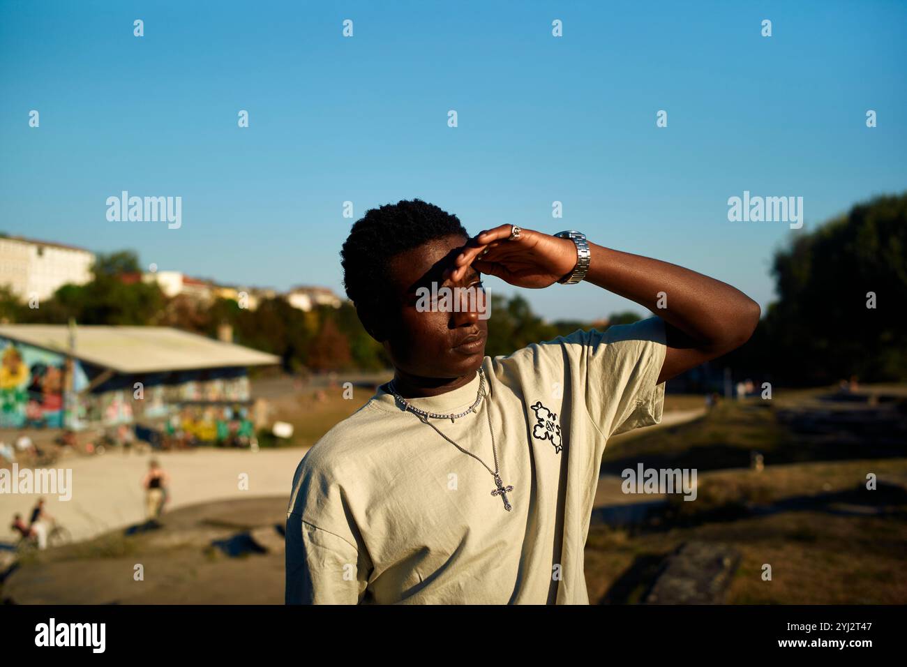 A young man shielding his eyes from the sun with his hand in a public ...