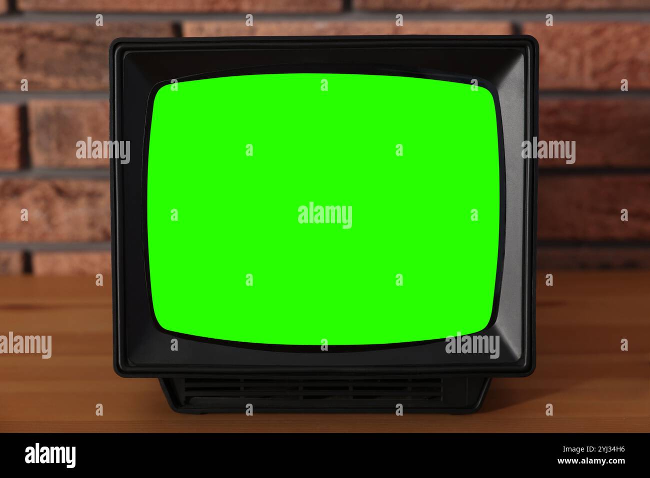 Retro Tv set with green screen on wooden table near brick wall. Chroma ...