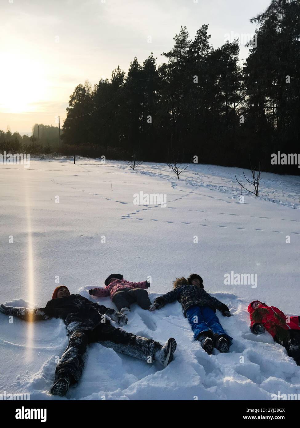 Four children lie joyfully on fresh snow, making snow angels under a ...