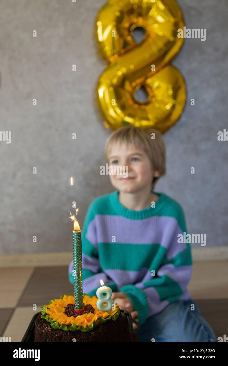 cute dreamy birthday boy looks at the cake and burning candles, number ...