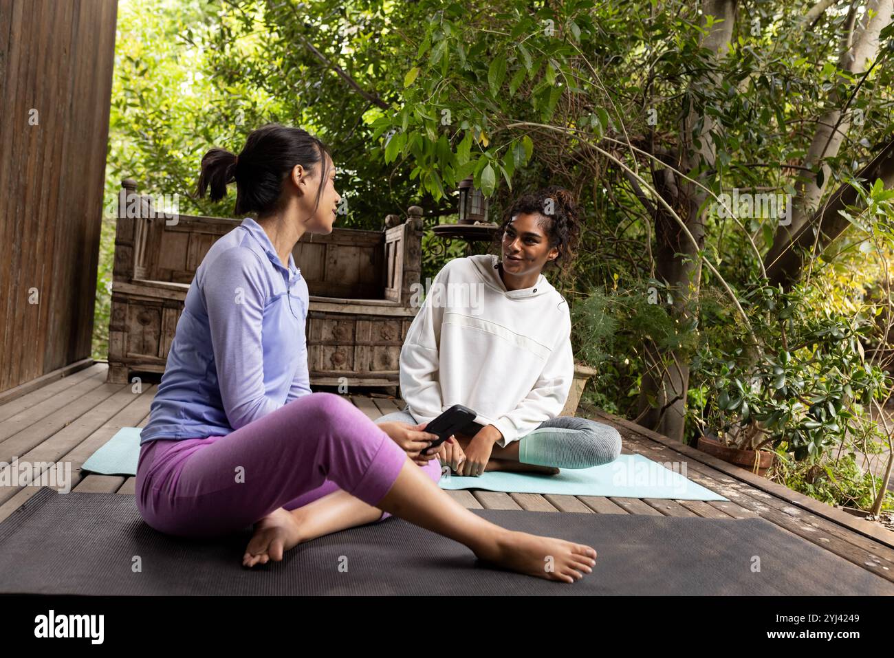 multiracial female friends relaxing on yoga mats on deck, enjoying ...