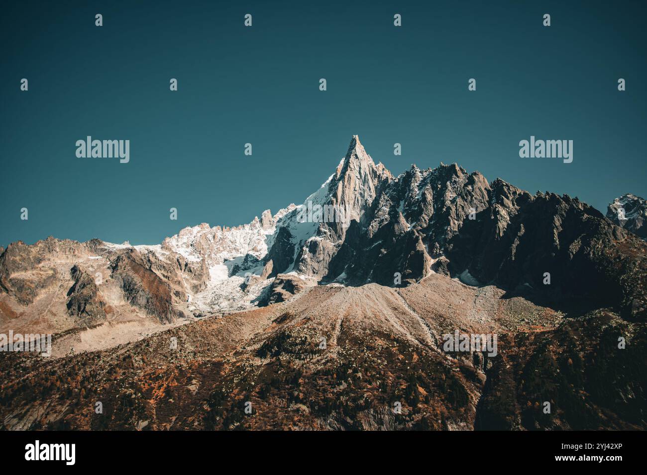 Majestic mountain peak with rugged rocky terrain and snow-capped summits under a clear blue sky ...
