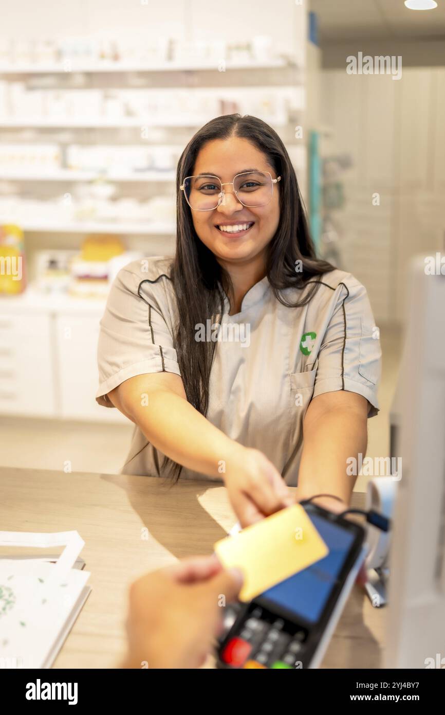 Vertical photo of a smiling pharmacist attending a client while paying ...