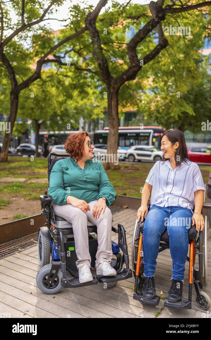 Two multi-ethnic disabled female friends in wheelchair talking in a ...