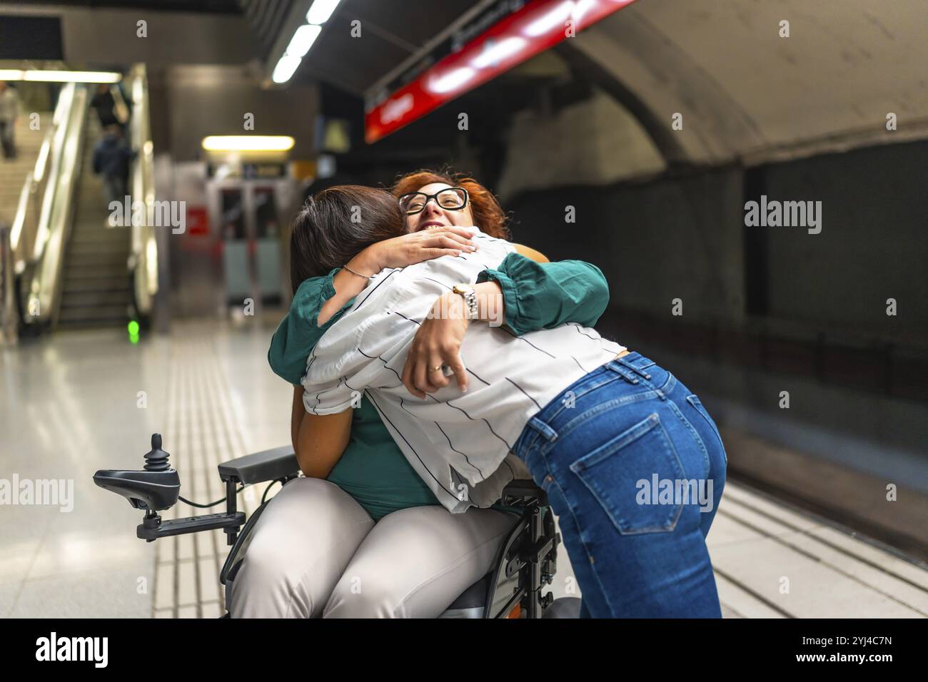 Joyful woman hugging a disabled friend in wheelchair in the subway ...