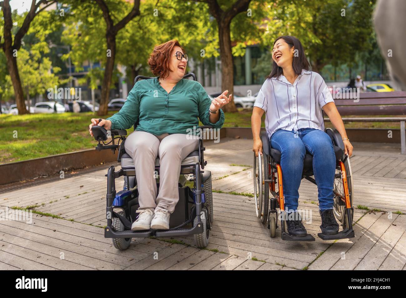 Two multiracial women with disability in wheelchair laughing talking ...