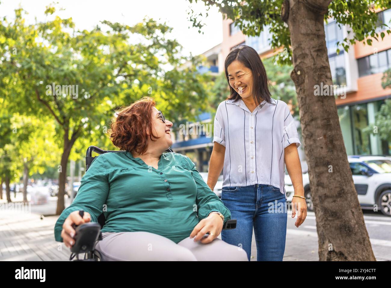 Asian woman and friend with disability talking and walking along a ...