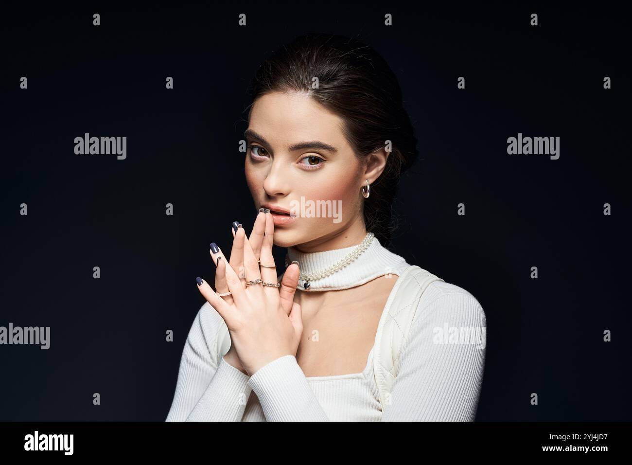 A young woman poses elegantly with a contemplative expression, hands ...