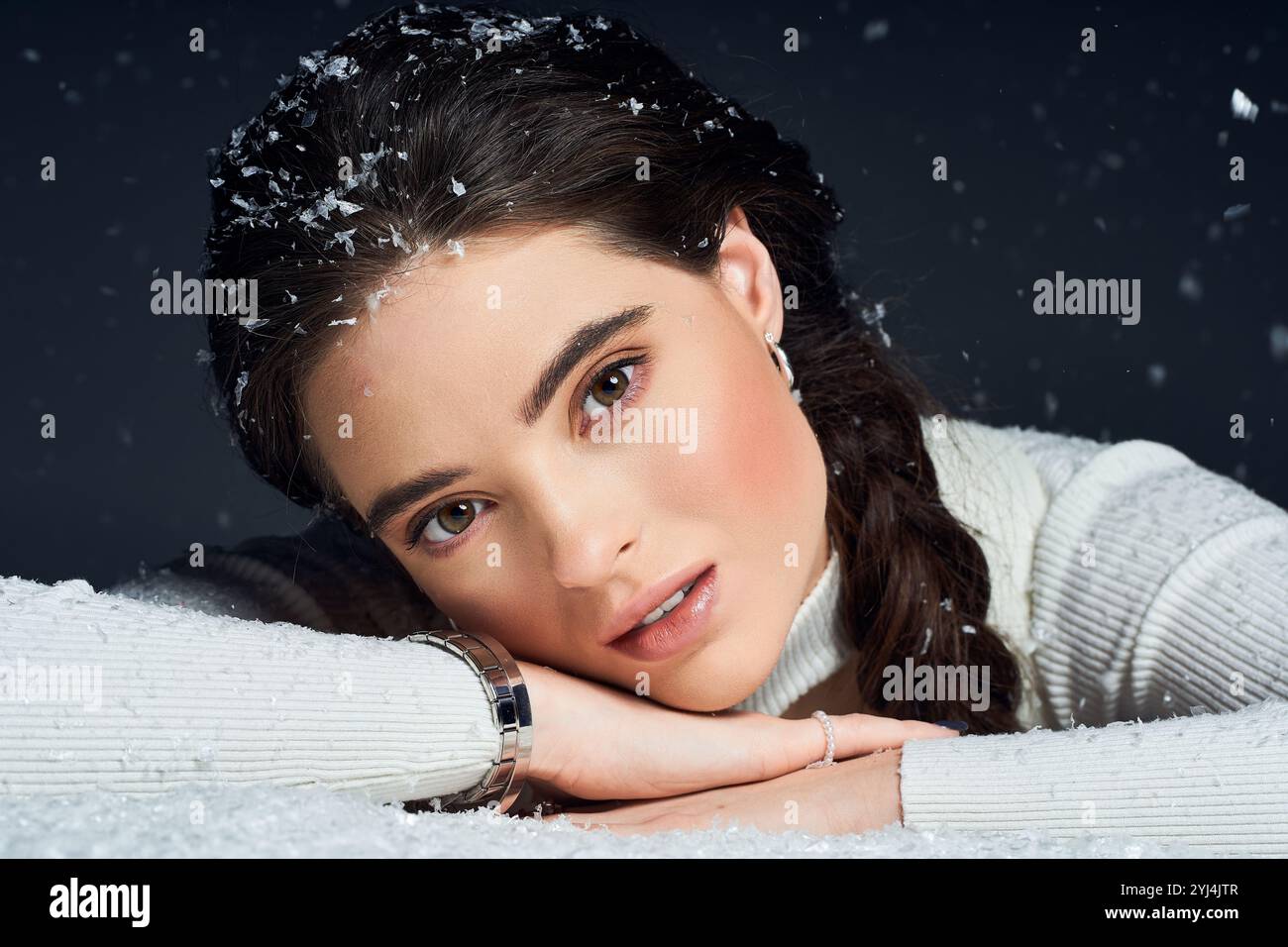 A captivating woman rests on a snowy surface, gazing thoughtfully while ...