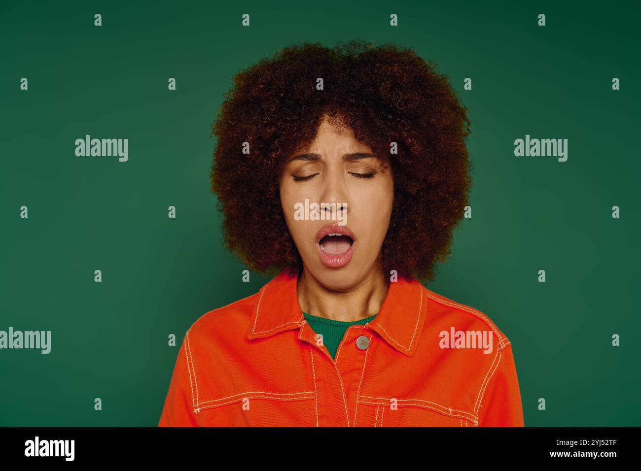 A pretty young woman with curly hair yawning while dressed casually in ...
