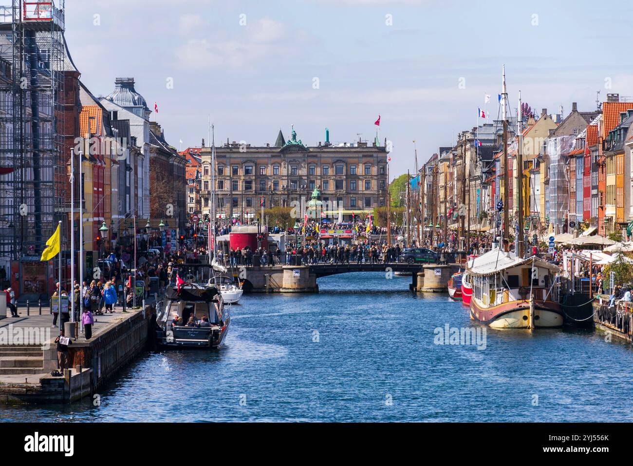 People walk past colorful facades and old ships along the Nyhavn canal ...