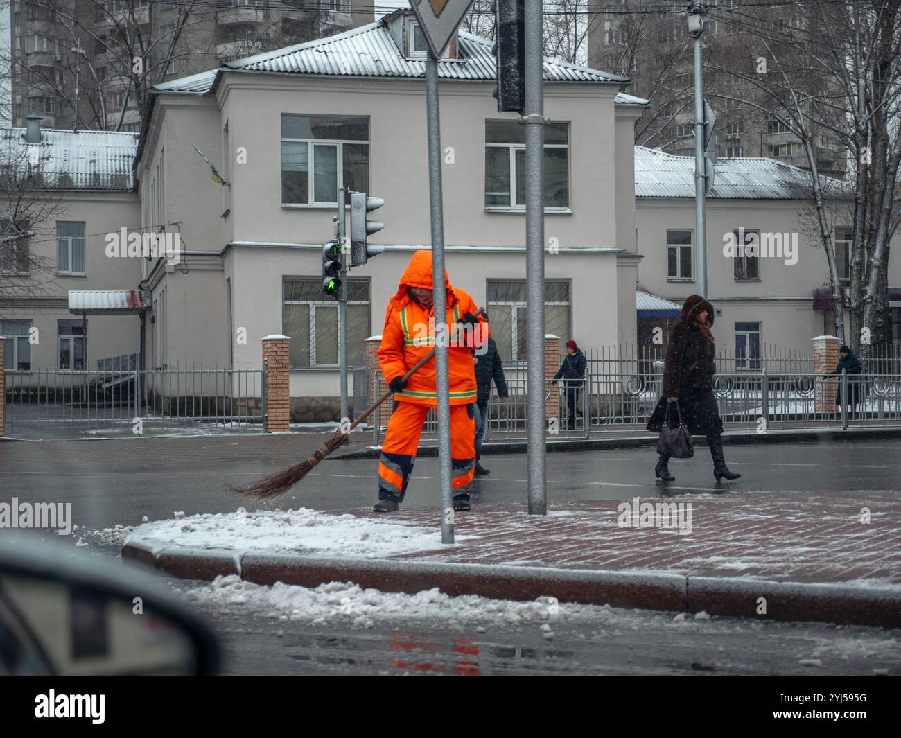 Municipal street cleaner in orange uniform with a broom sweeps snow at ...