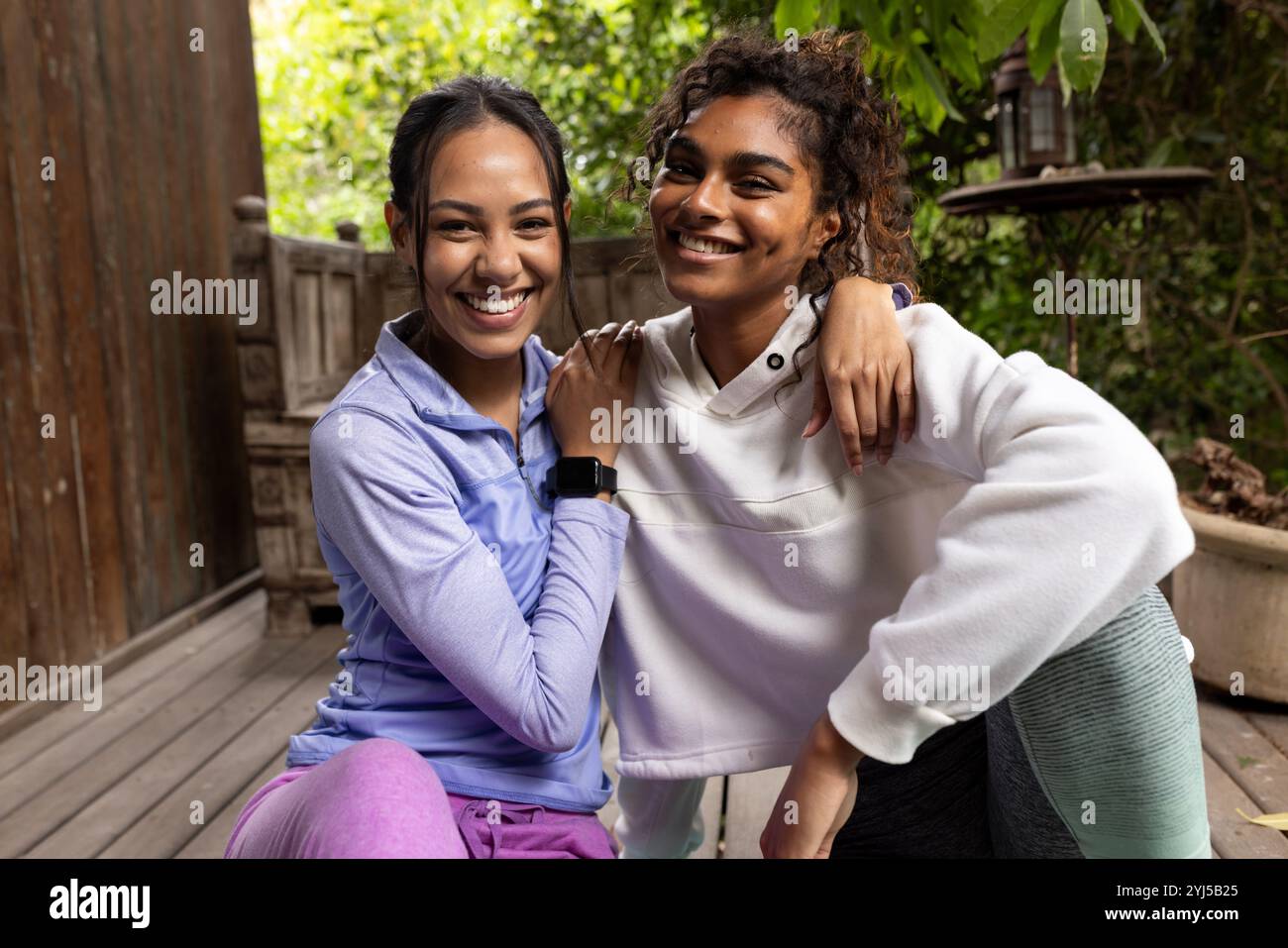 Sitting on deck, two multiracial female friends embracing and smiling ...