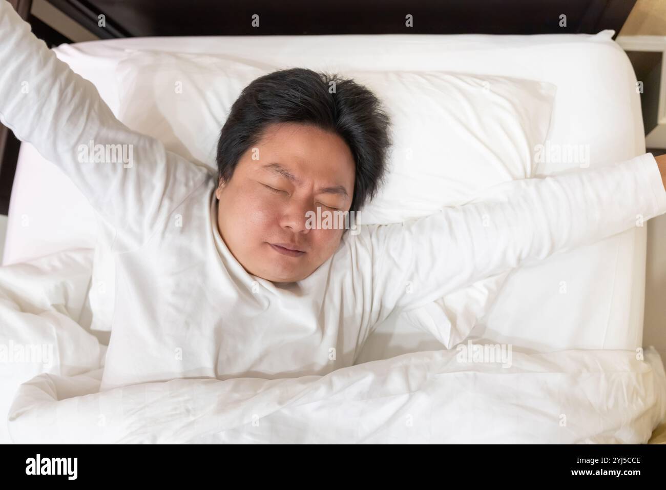 An Asian man begins his day with a refreshing stretch on the bed ...