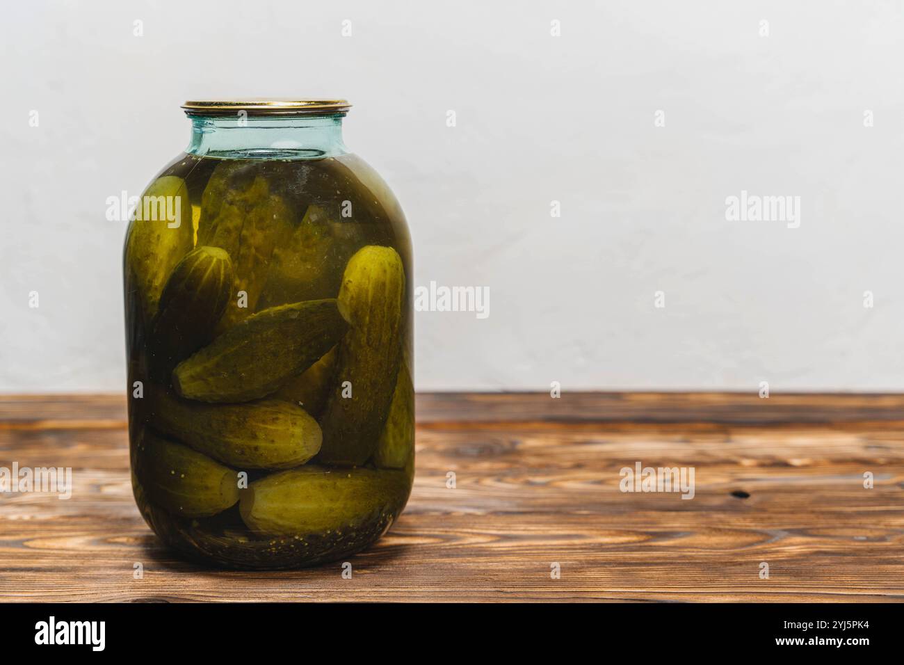 A standard-sized glass jar filled with pickles is placed atop a rustic ...