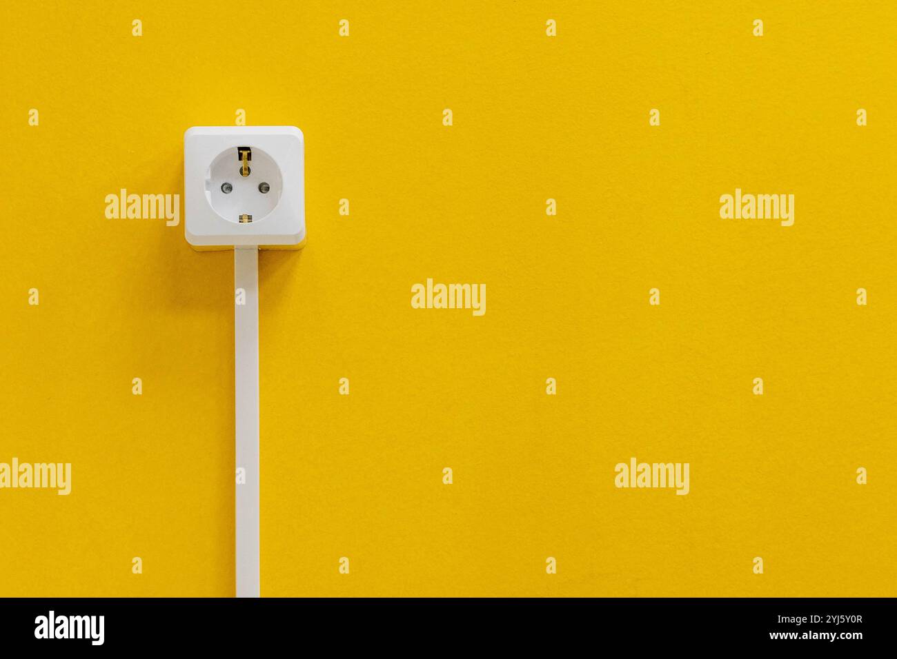 A white electrical socket is affixed to a bright yellow wall. copy ...