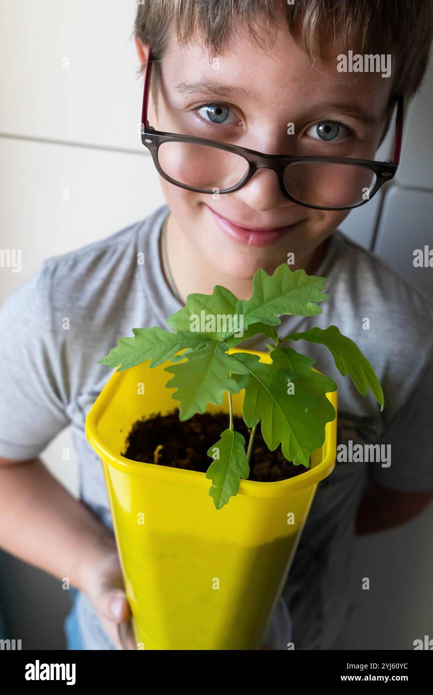 Young boy proudly holding a potted oak sapling, symbolizing ...