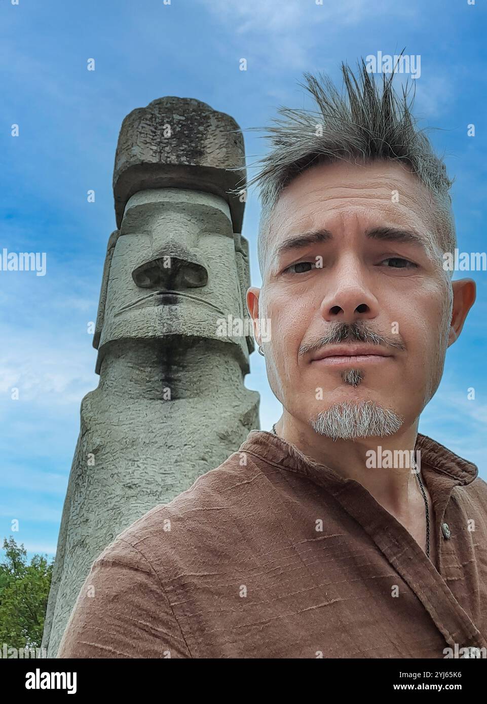Man posing in front of a stone Moai statue, both looking directly at ...