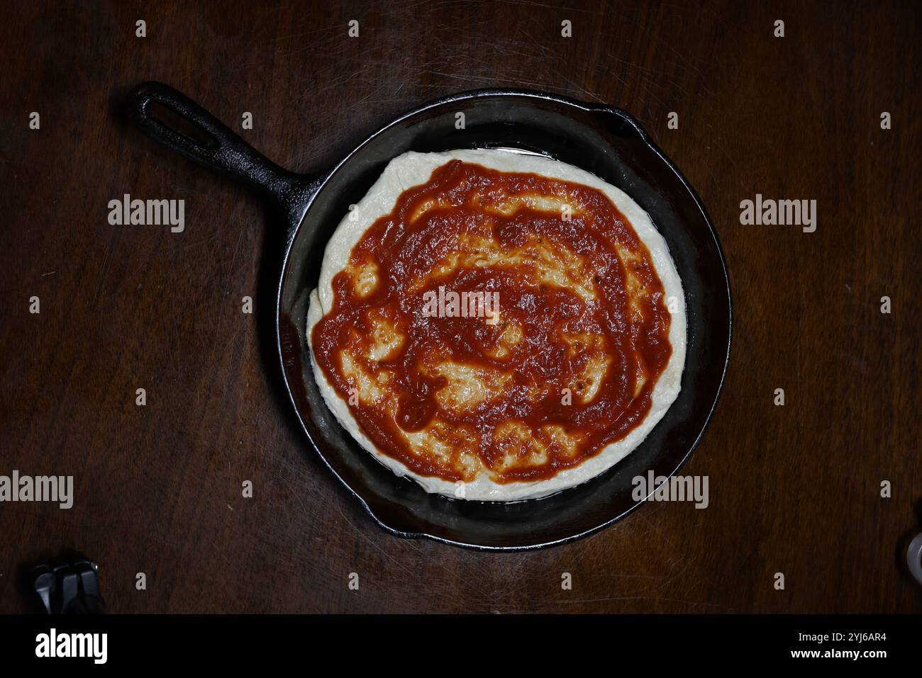 small pizza dough pressed into a cast iron pan, with pizza sauce spread ...