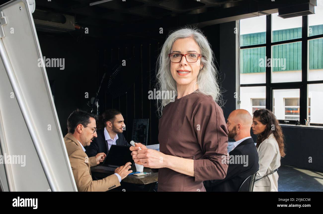 A confident businesswoman stands beside a whiteboard, presenting ideas ...