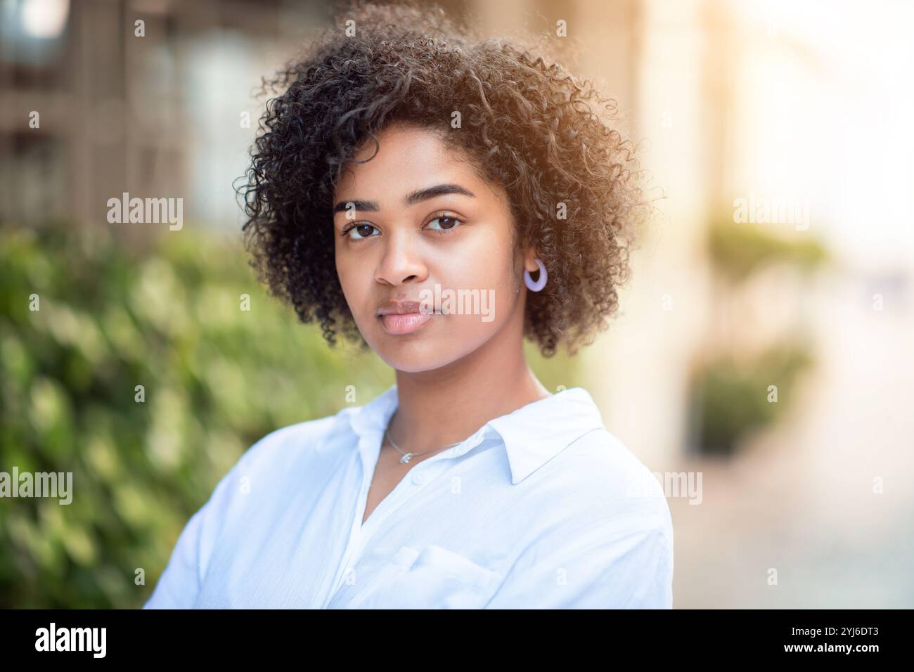 A young woman stands with a relaxed demeanor, showcasing her curly hair ...