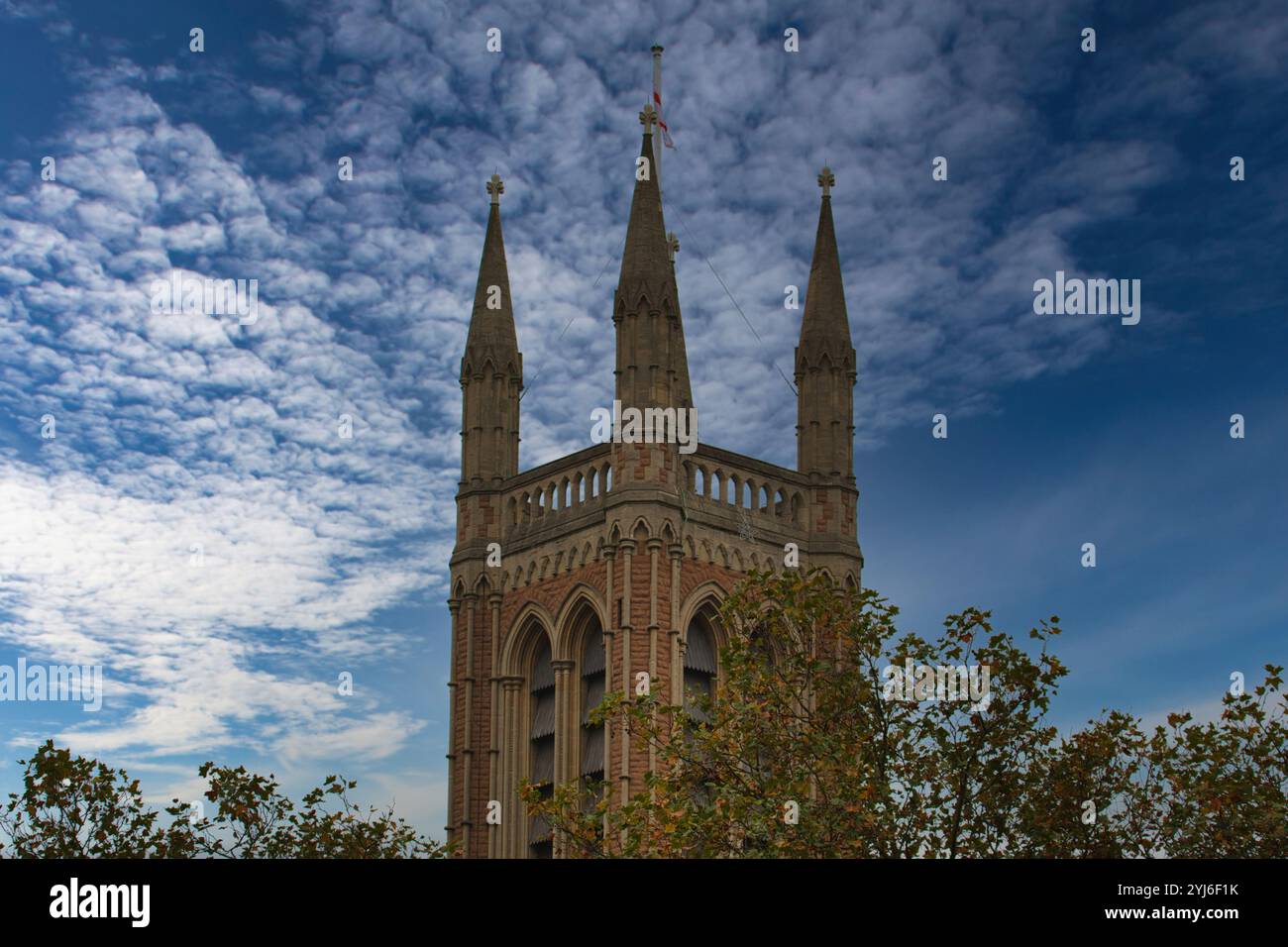 A low angle view of a stone church tower with three spires and a flag ...