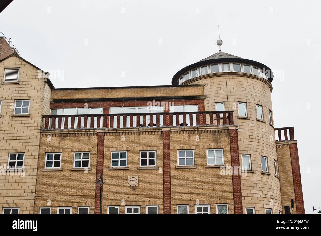 A tan brick building with a rounded corner tower featuring a dark gray ...