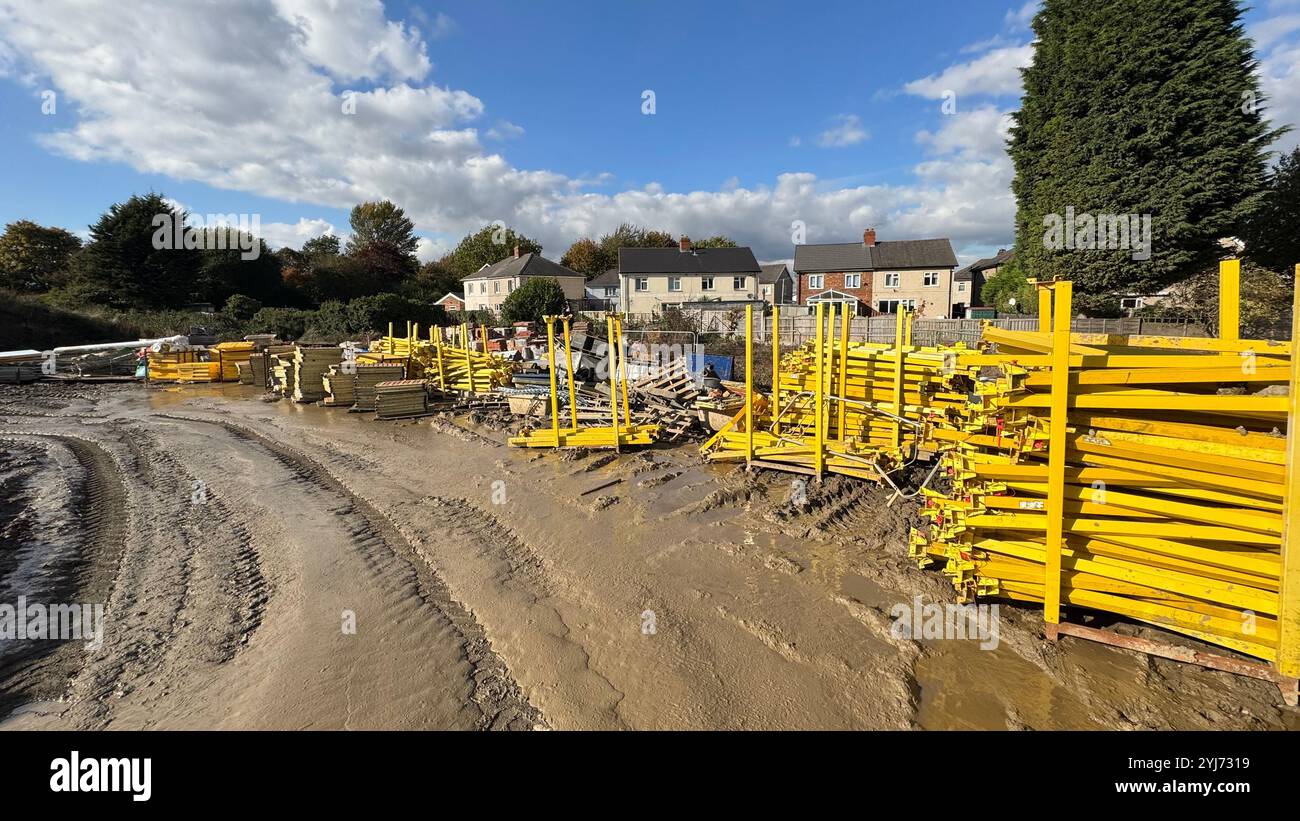 A muddy construction site with scattered yellow scaffolding beams and ...