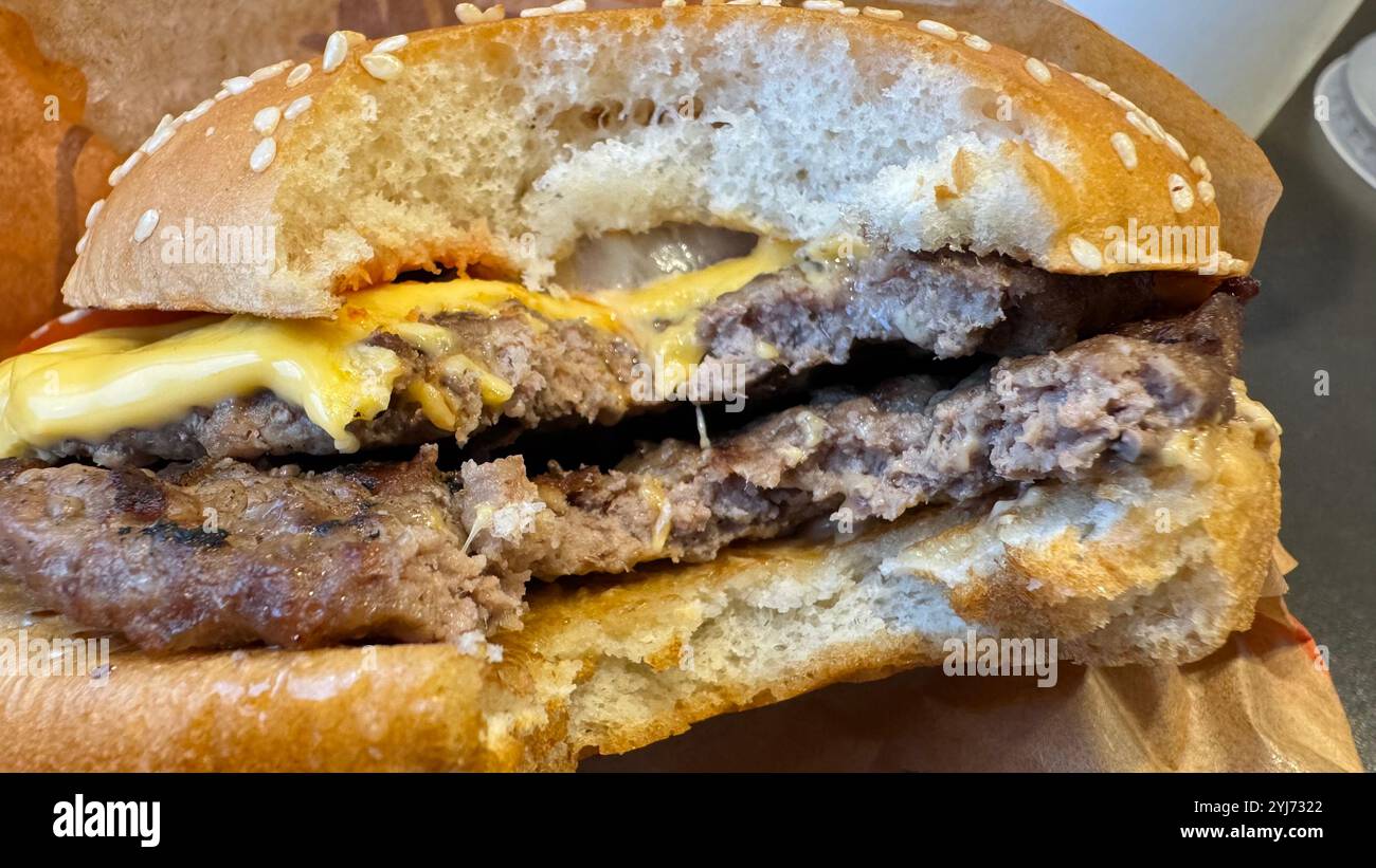 A partially eaten double cheeseburger on a sesame seed bun, with two ...