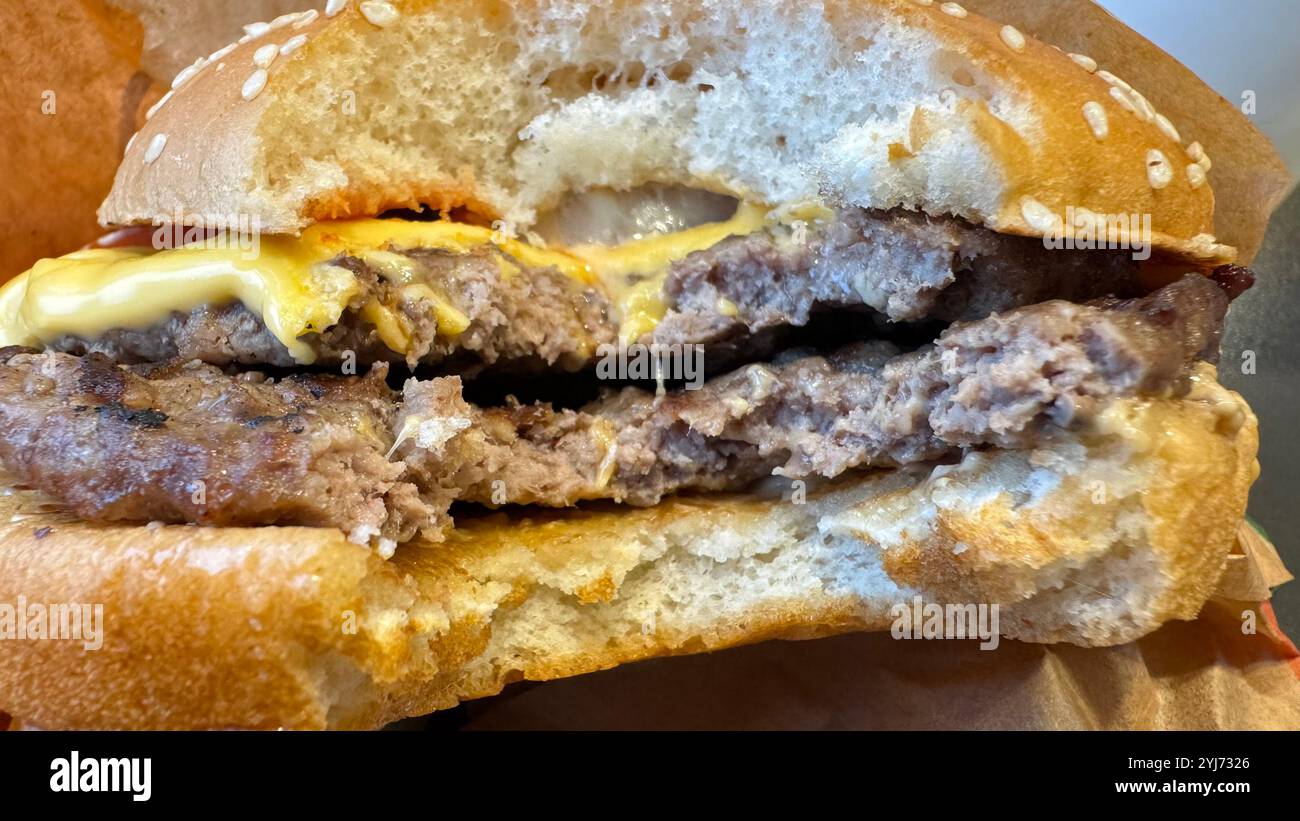 A close-up shot of a double cheeseburger, partially eaten, showing two ...