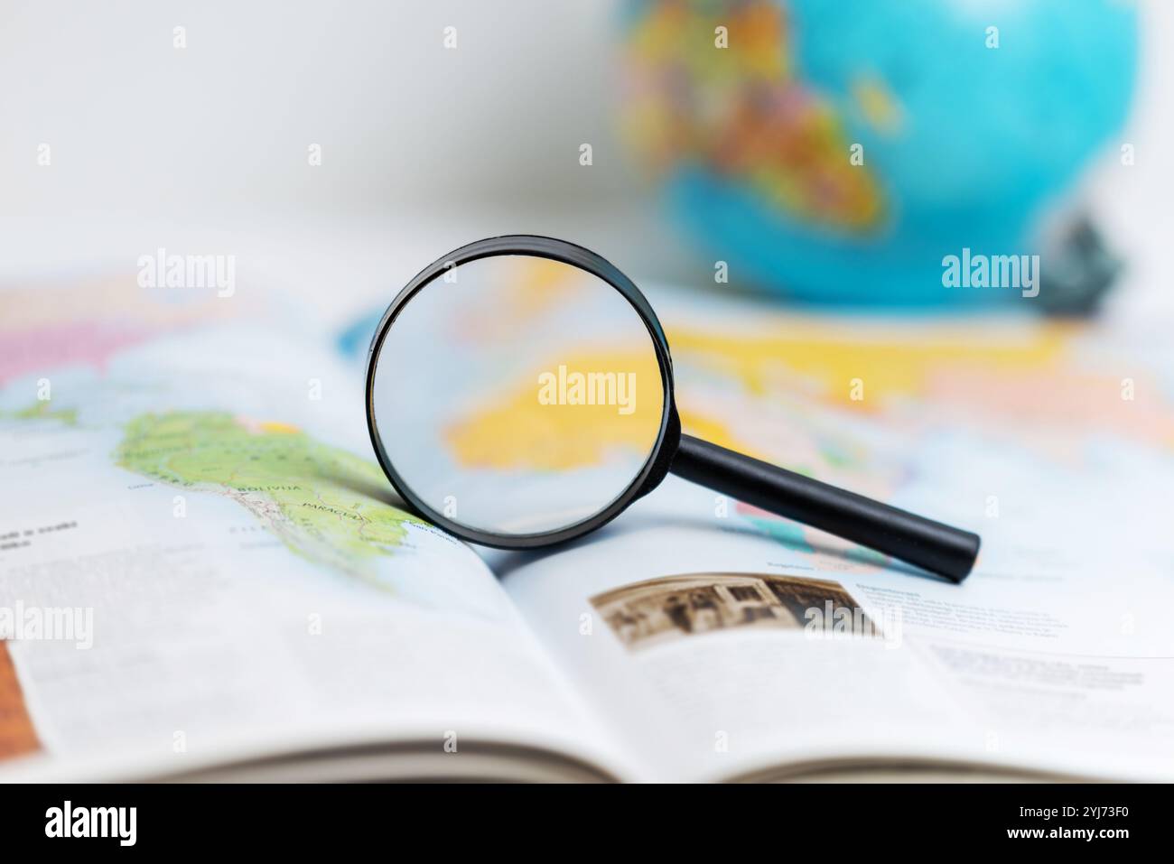 Magnifying glass on atlas with globe in background, symbolizing ...