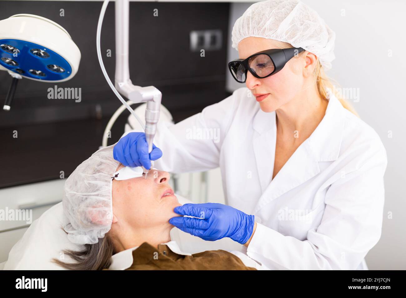 Female beautician making laser resurfacing of aged female client Stock ...