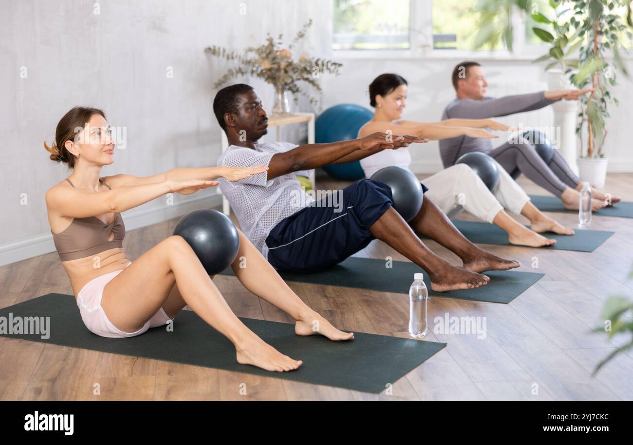 Group of active people doing soft ball pilates exercises during group ...